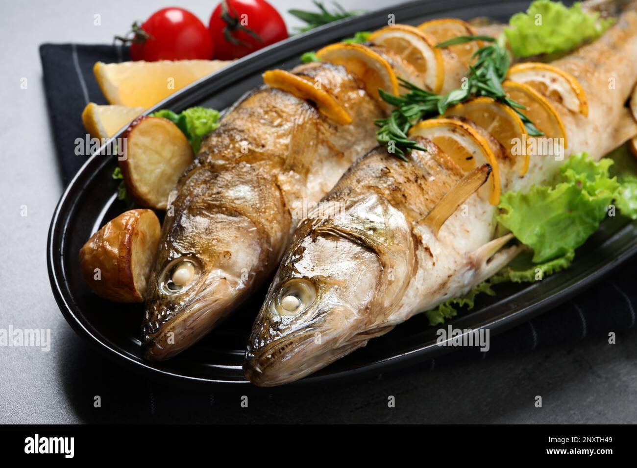 Tasty homemade roasted pike perches with garnish on grey table, closeup ...