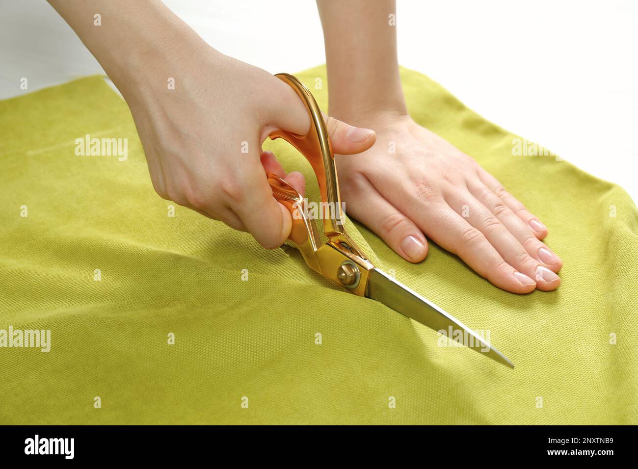 Seamstress cutting light green fabric with scissors at workplace ...