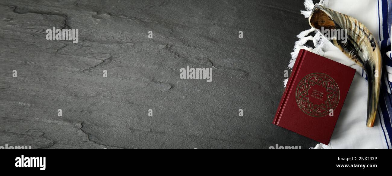 Tallit, shofar and book Torah with text in Hebrew on black table, flat ...