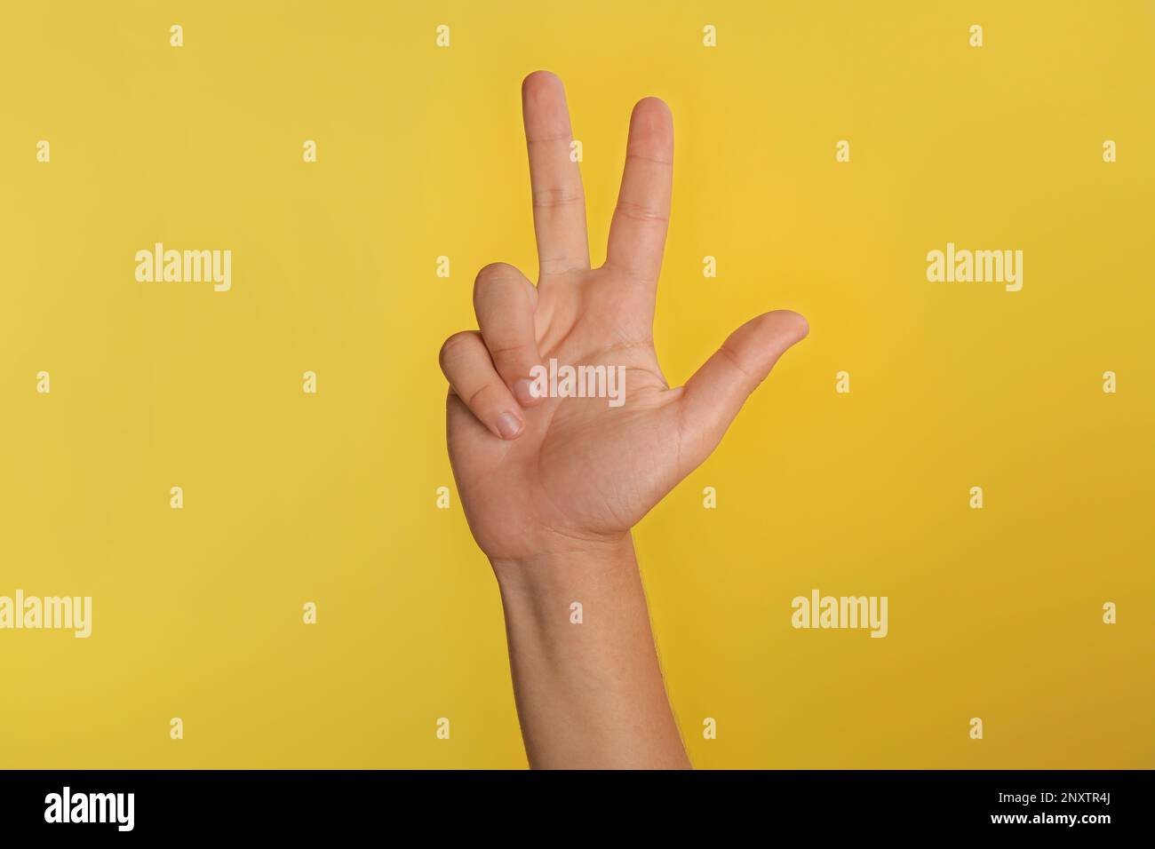 Teenage boy showing three fingers on yellow background, closeup Stock ...