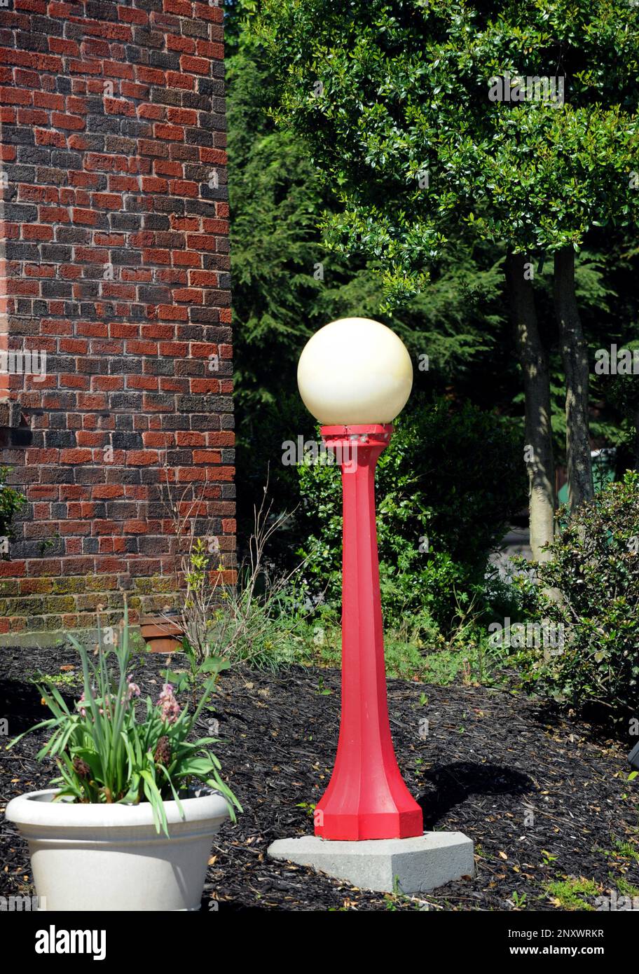 Red metal lamp post has a round white globe. It is sitting in a garden ...