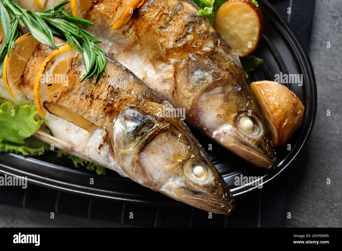 Tasty homemade roasted pike perches with garnish on grey table, closeup ...