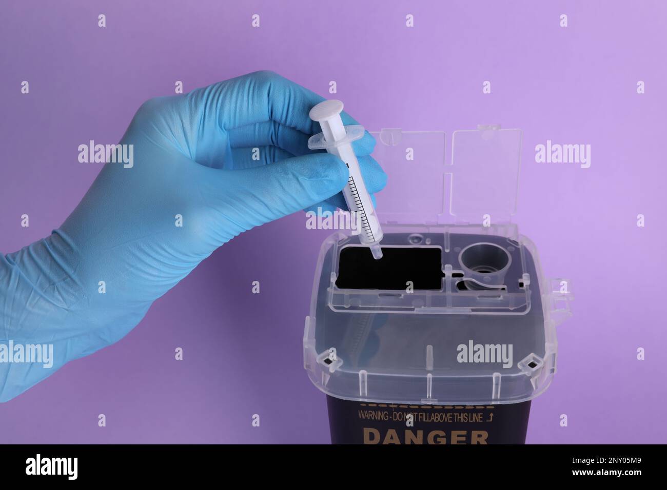 Doctor throwing used syringe into sharps container on violet background ...