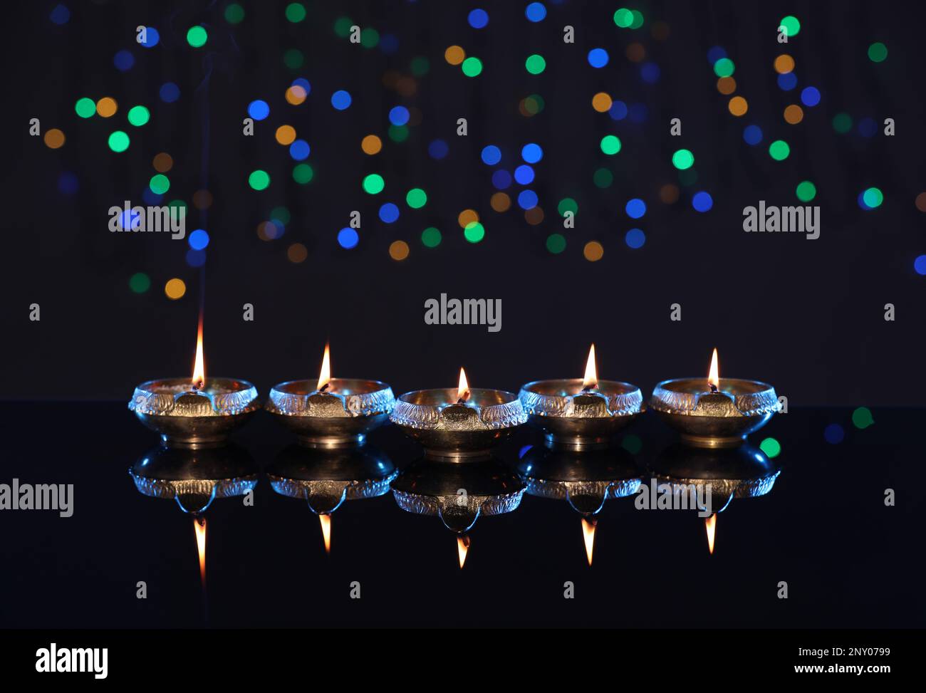 Many lit diyas on dark background with blurred lights, space for text ...