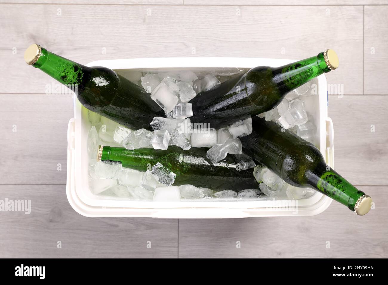 Plastic cool box with ice cubes and beer on wooden floor, top view ...