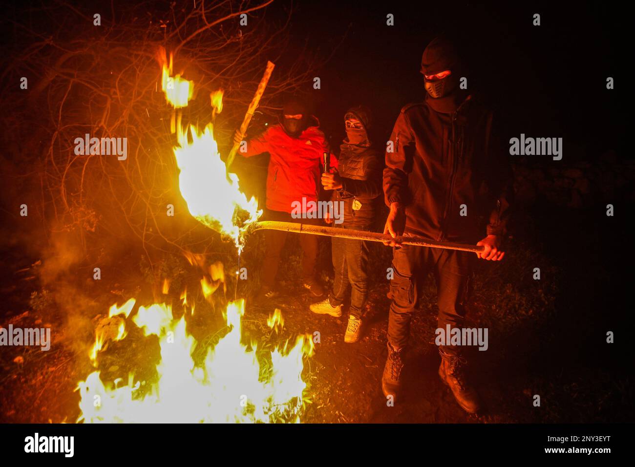 Masked Palestinians carrying wooden sticks around the fire stand on ...