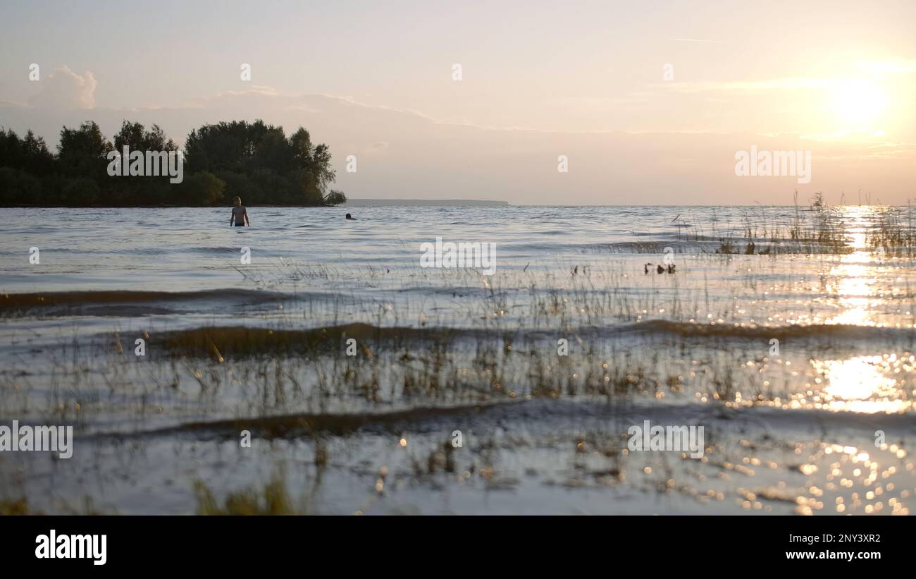 Silhouettes of floating people in village lake at sunset. Creative ...