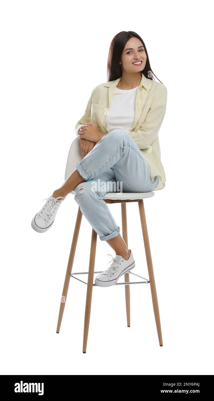 Beautiful young woman sitting on stool against white background Stock ...