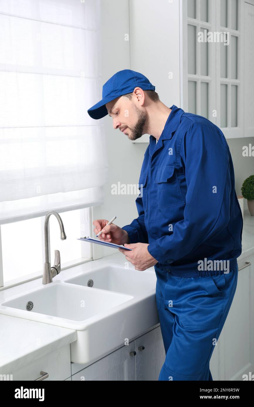 Professional plumber with clipboard checking water tap in kitchen Stock ...