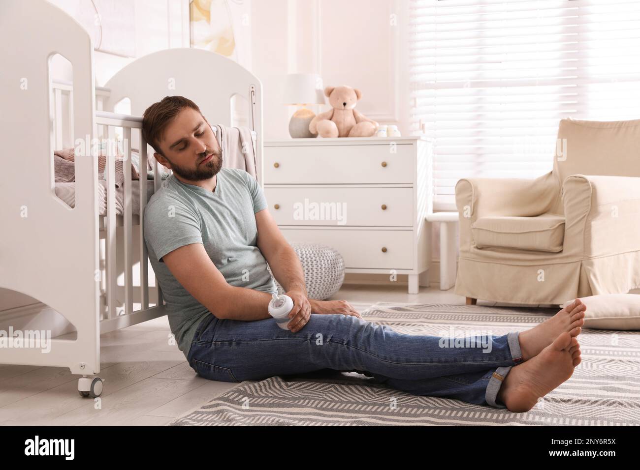 Tired father with bottle of milk sleeping on floor in children's room ...