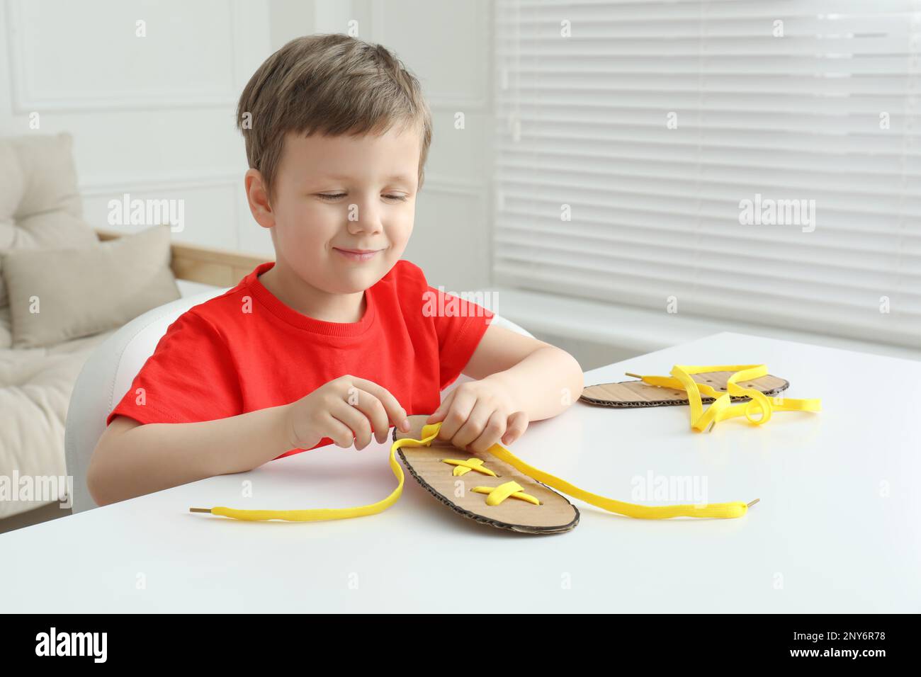 Little boy tying shoe lace using training cardboard template at white ...