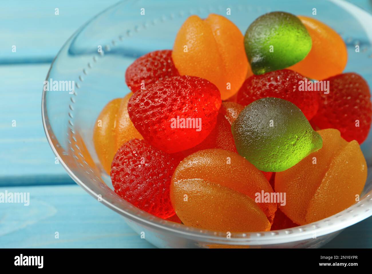 Delicious gummy fruit shaped candies in glass bowl on light blue table ...