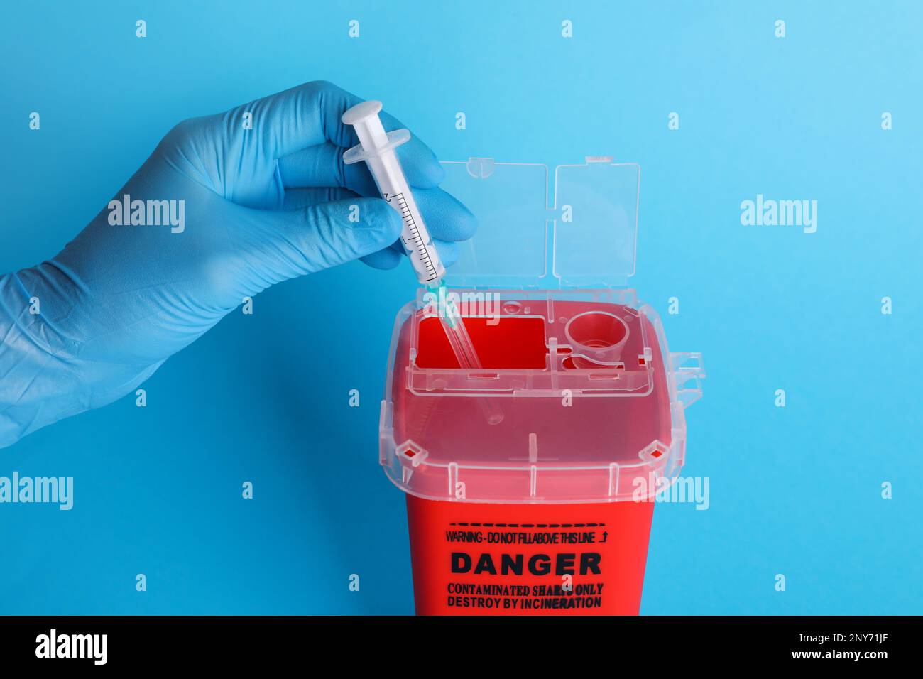 Doctor throwing used syringe into sharps container on light blue ...