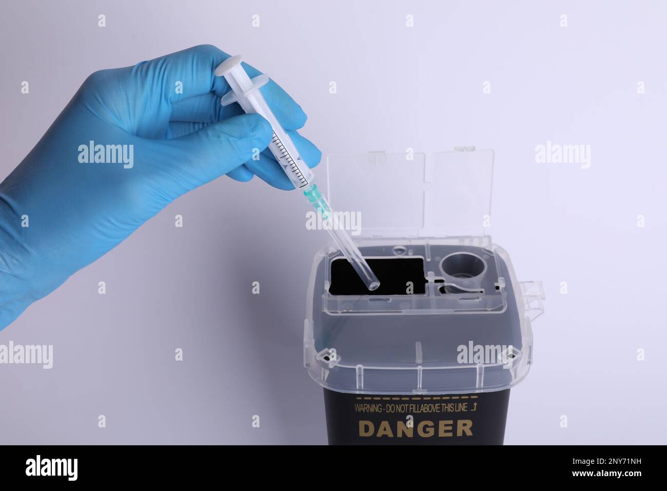 Doctor throwing used syringe into sharps container on white background ...