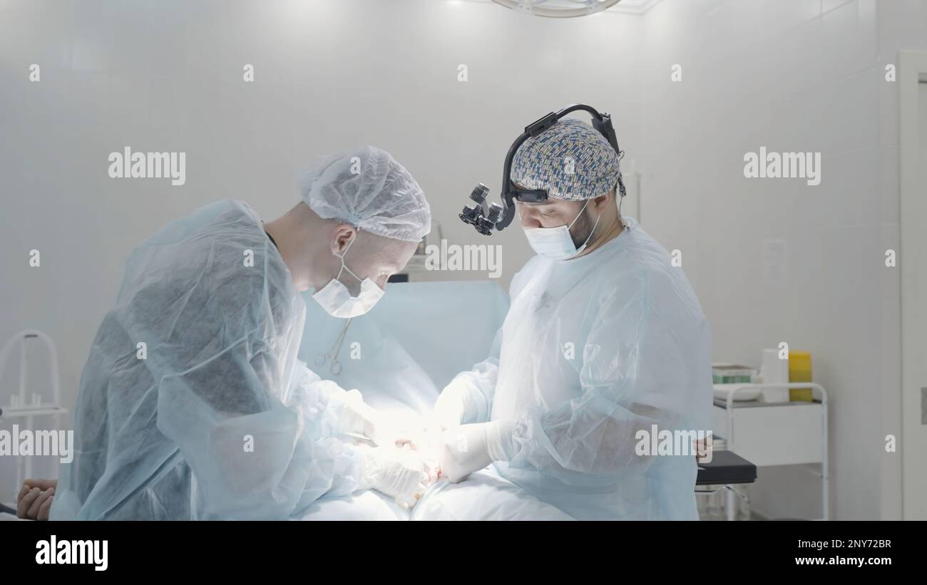 Side view of male surgeons in the operating room of a hospital. Action ...