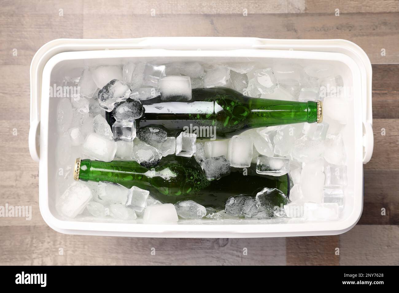Plastic cool box with ice cubes and beer on wooden floor, top view ...