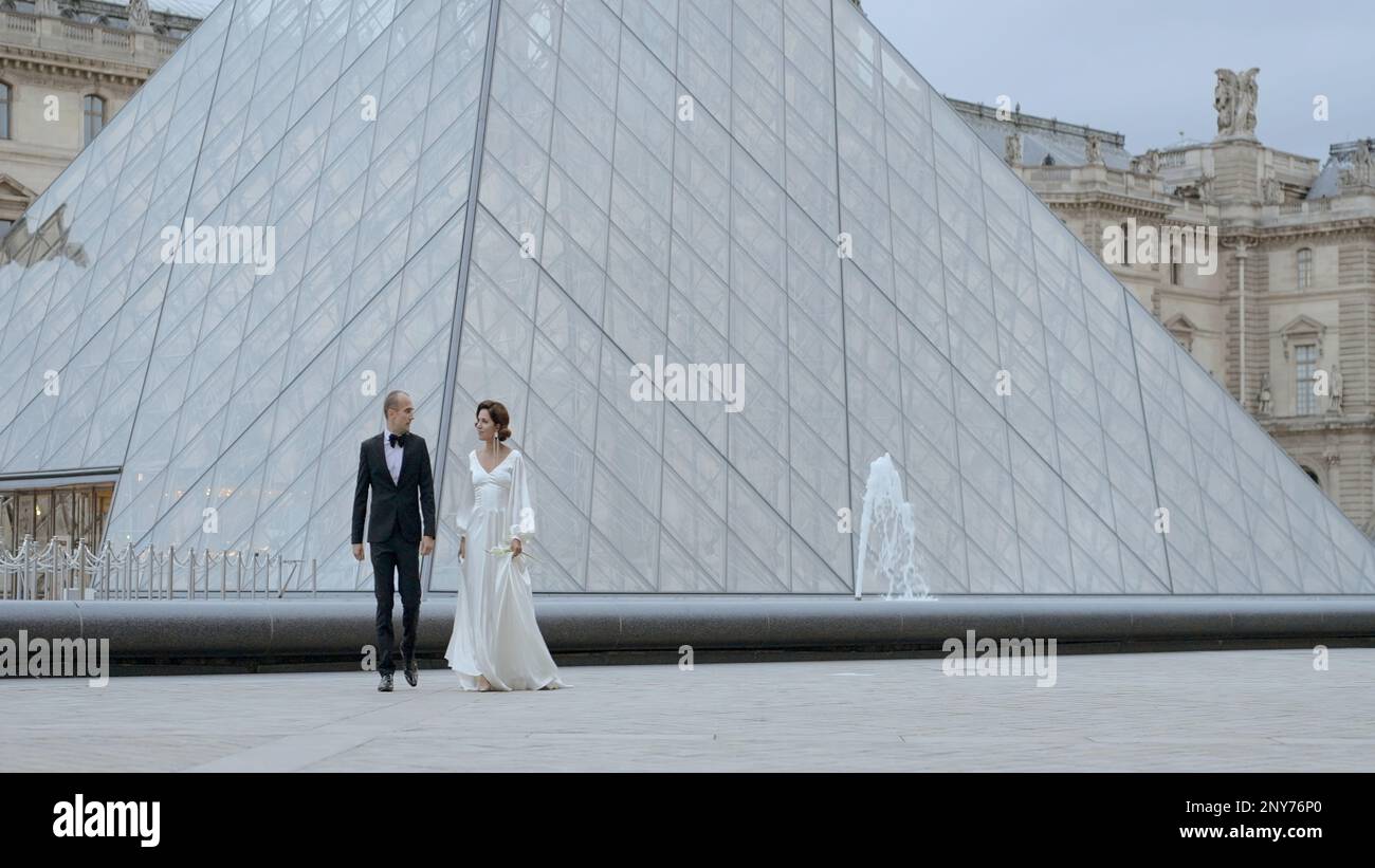 Wedding couple walking on the background of the Louvre pyramid, France ...