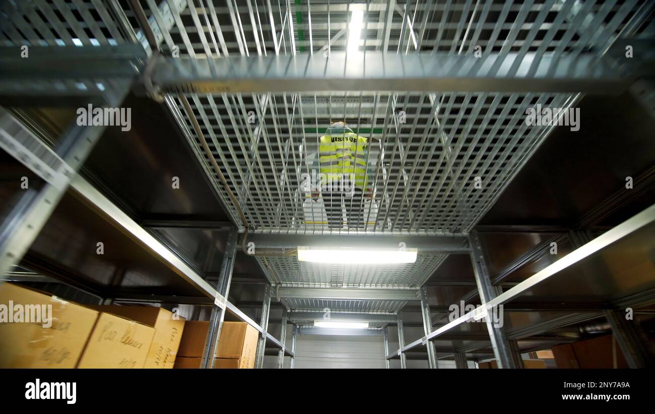 Bottom view of a worker in bright uniform walking on metal grid floor ...
