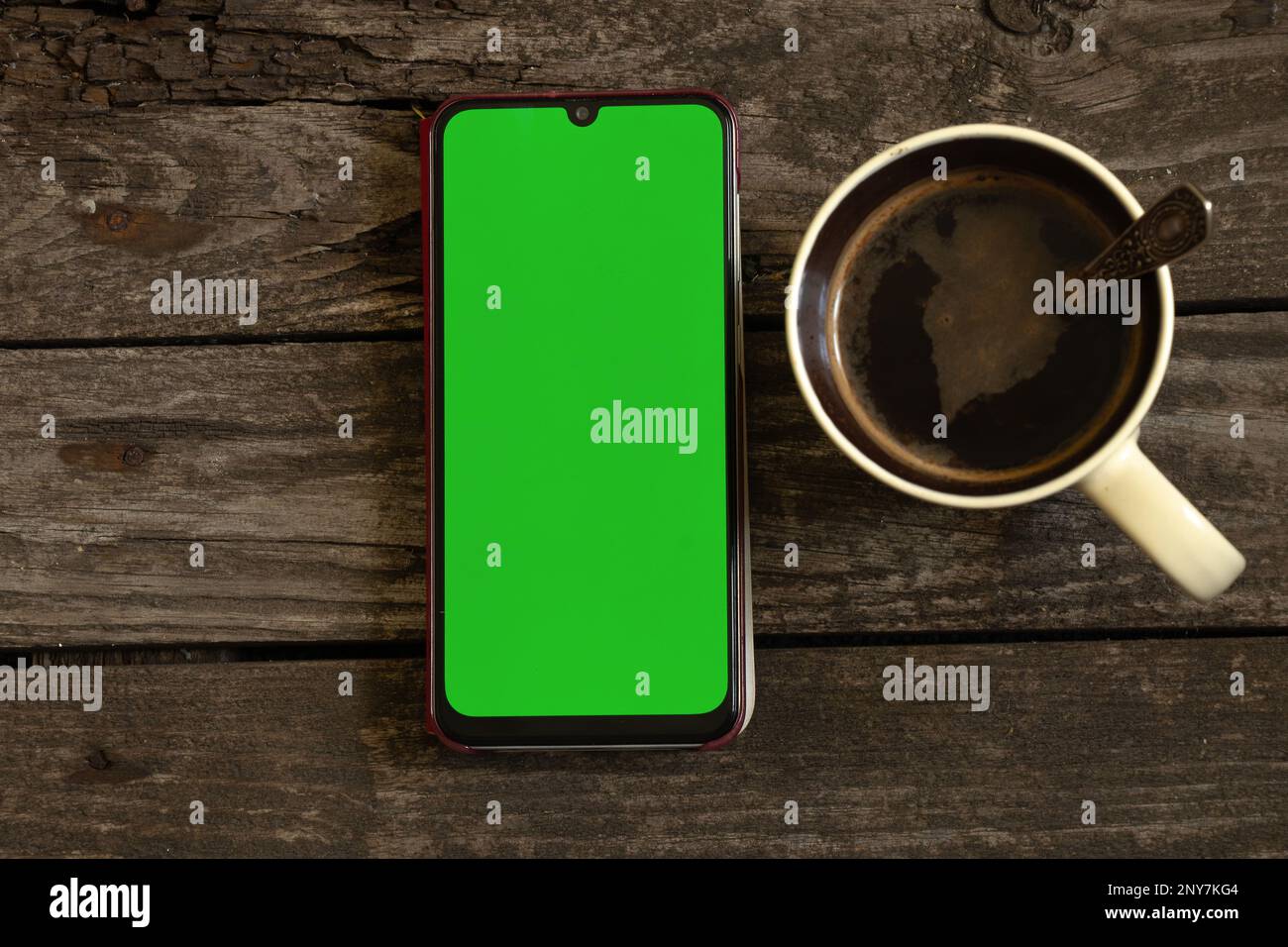 a phone with a green screen lies on an blackboard and next to a cup ...
