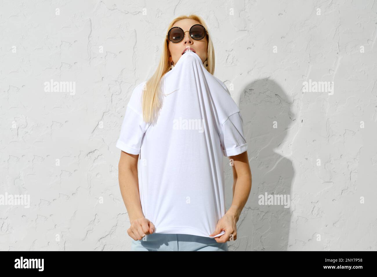 Playful blonde woman bites the collar of a t-shirt Stock Photo - Alamy