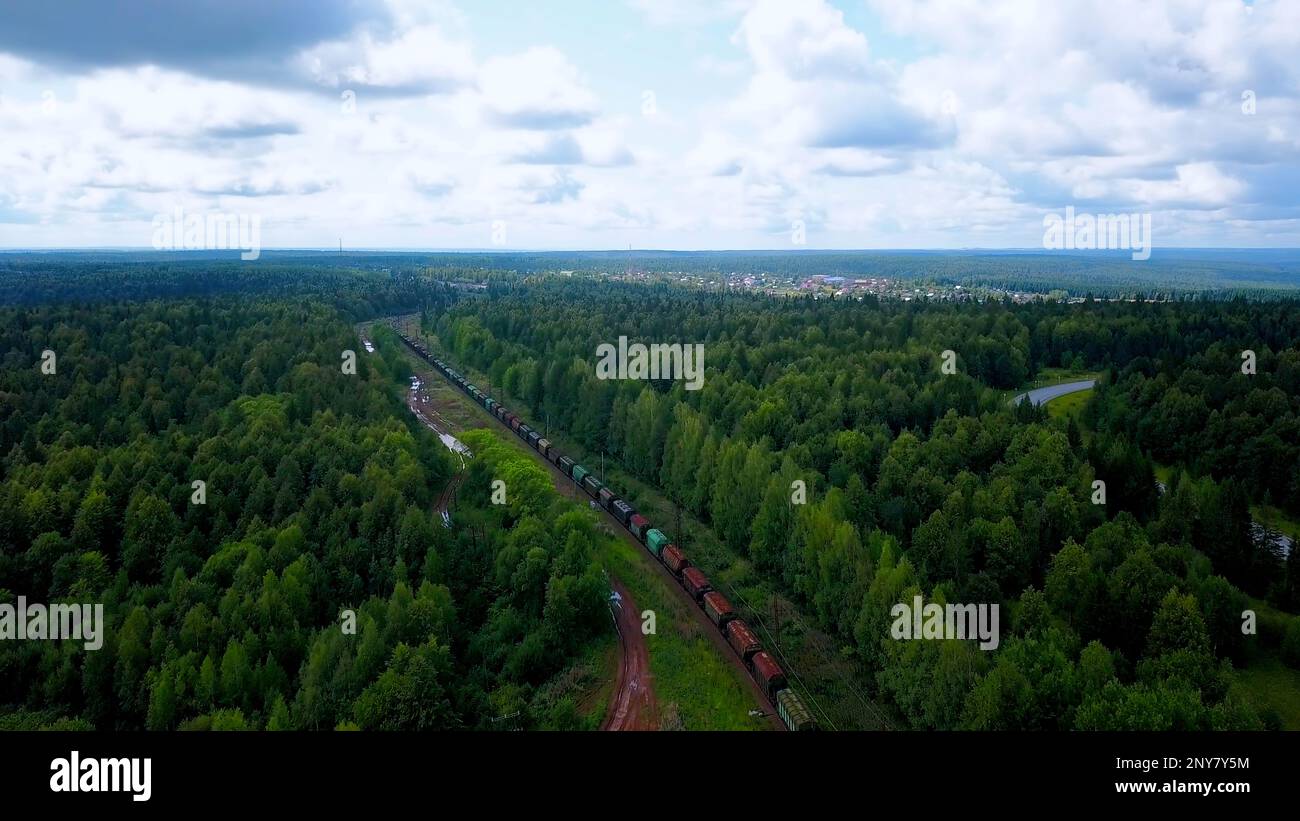 Aerial view of a long moving freight train along green summer trees ...