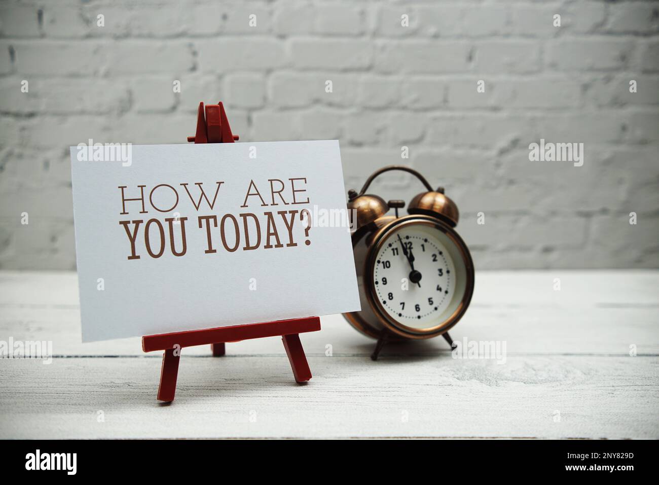 How are you today? text and alarm clock on white brick wall and wooden ...