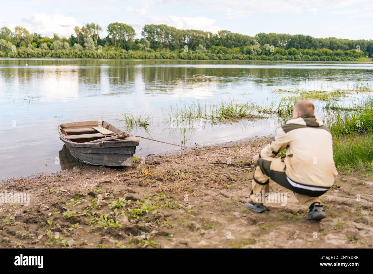 Rear view of unrecognizable fisherman wearing raincoat mooring oar boat ...