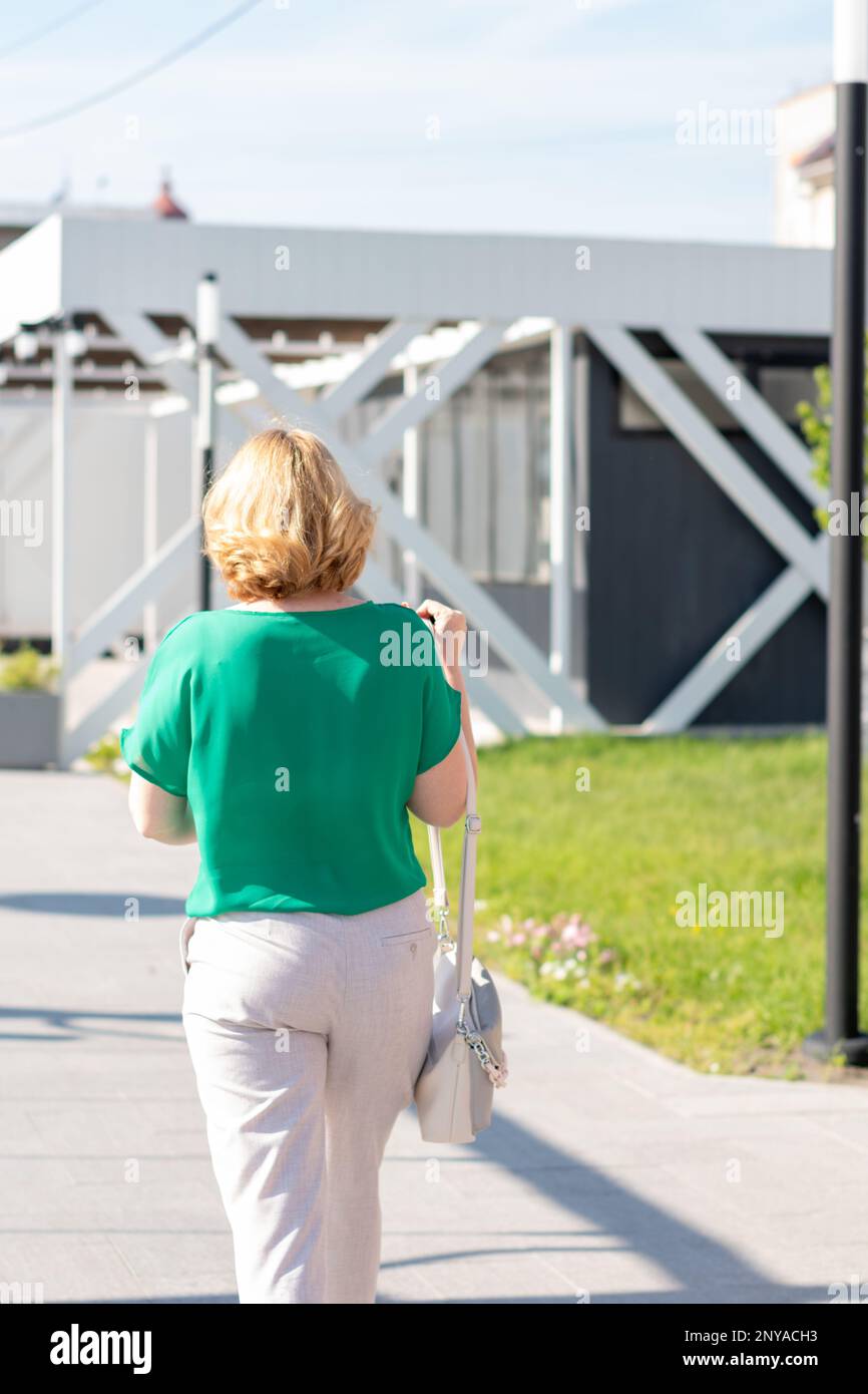 Rear view of a stylish slender woman in a green blouse, trousers and ...