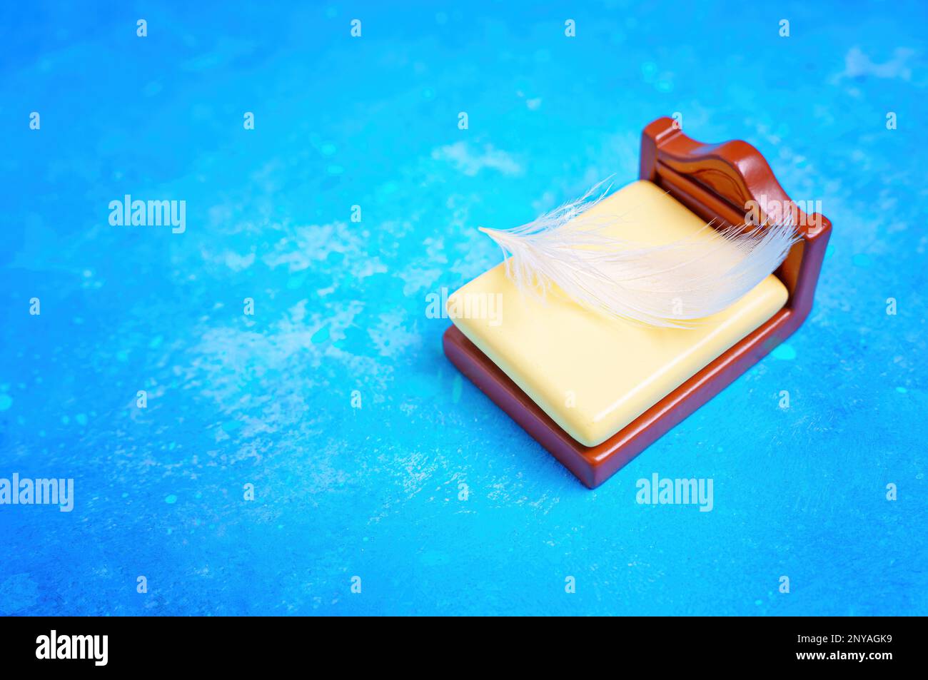 White feather rests on a miniature bed isolated on blue background with ...