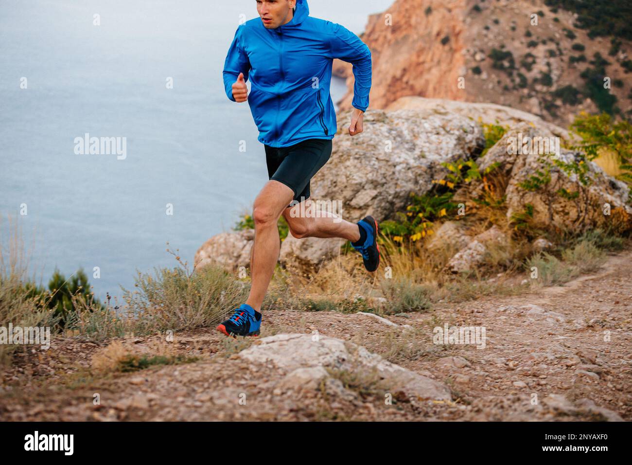 male runner running on mountain trail along sea Stock Photo - Alamy