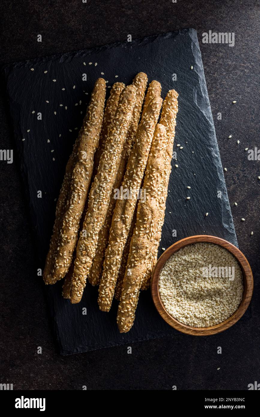 Italian grissini bread sticks with sesame seeds on the black table. Top ...