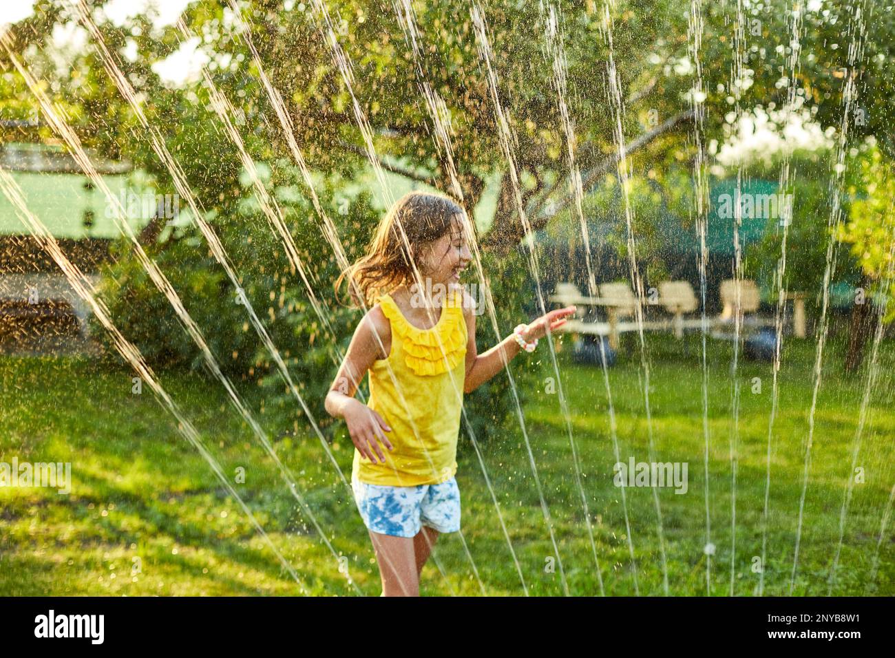 Happy kid girl playing with garden sprinkler run and jump, summer ...