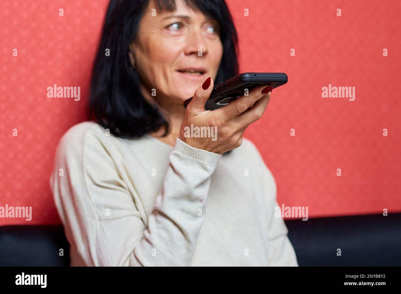 Senior woman sit on sofa speak to microphone dictate audio message on smartphone recorder talk ...