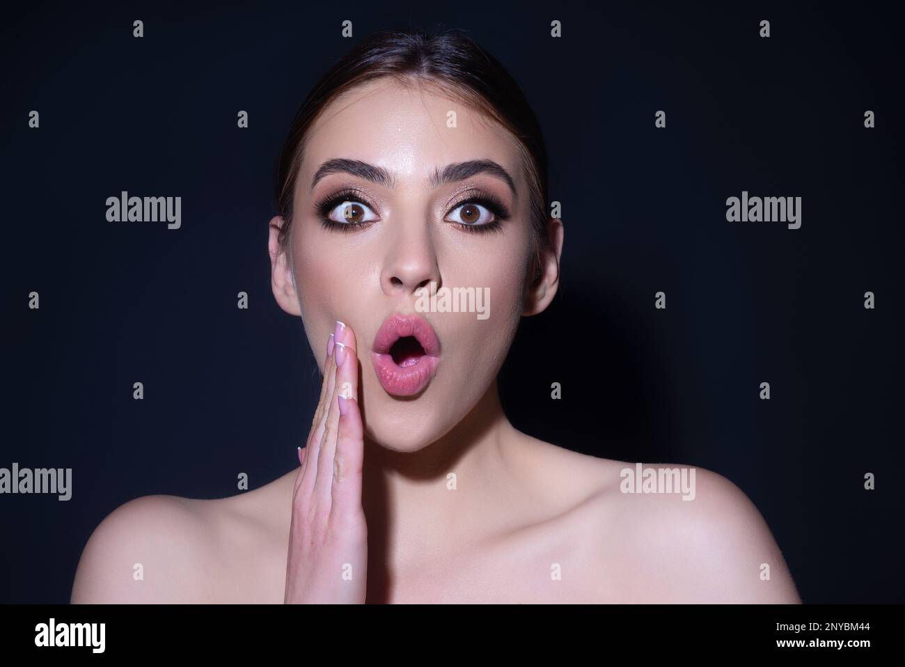Young surprised woman in t-shirt shouting wow, black studio background ...
