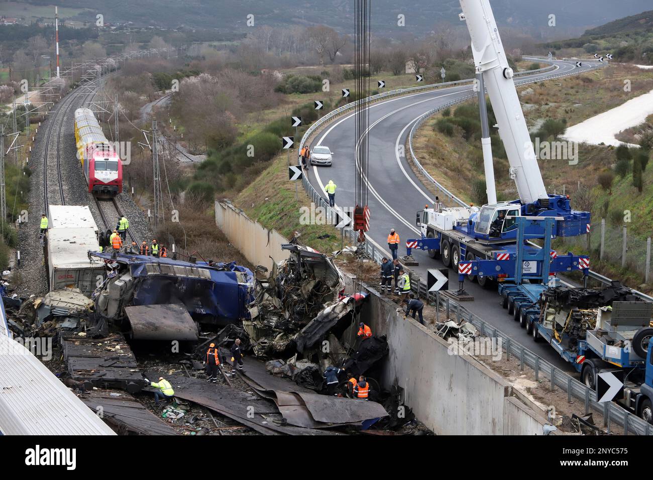 Workers supported by a crane try to remove debris from the rail lines ...
