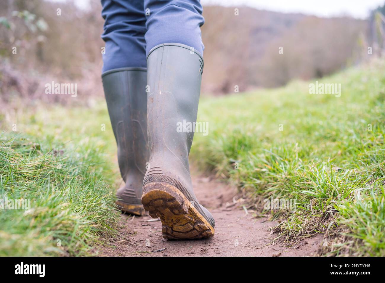 Low angle, rear view of a woman wearing green wellies walking outdoors ...