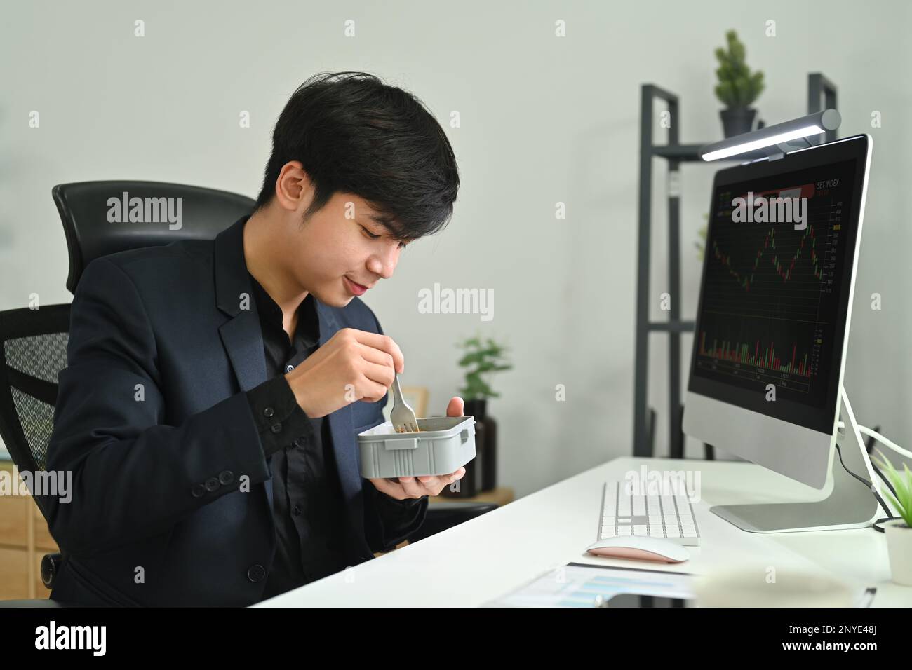 Happy asian man sitting at his office in front of computer screen and ...