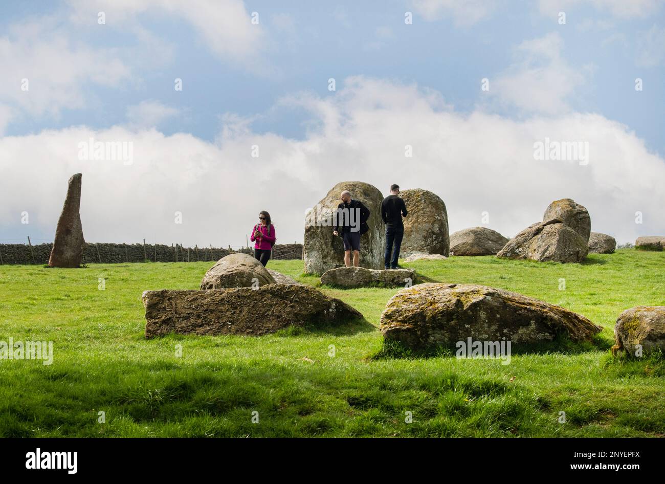 3 tourists looking at phones at Long Meg and Her Daughters stone circle ...