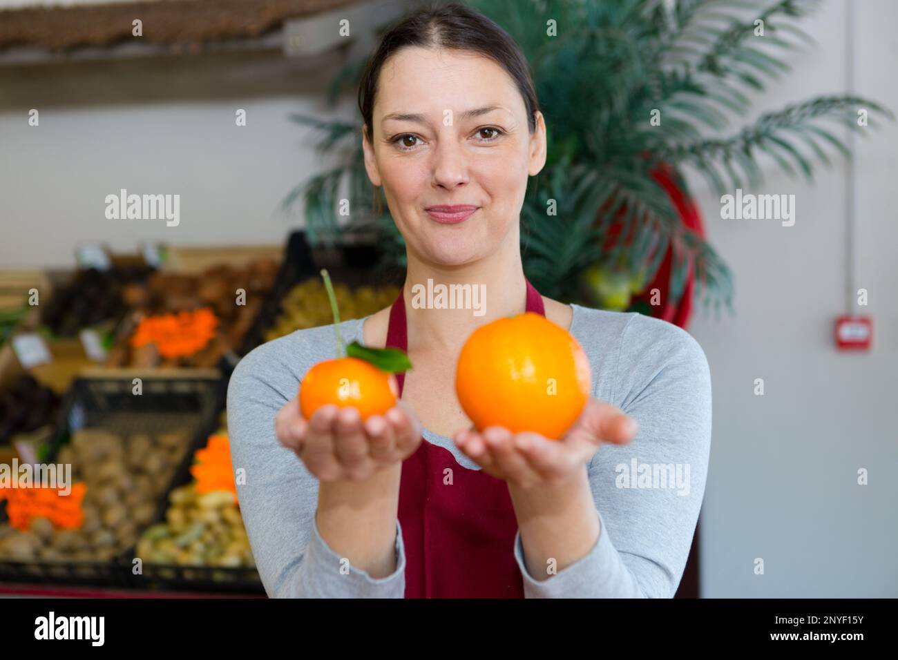 smiling supermarket worker in apron holding citrus in fruit section ...