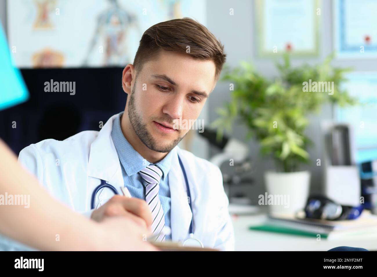Focused doctor working in medical office signing documents brought by ...