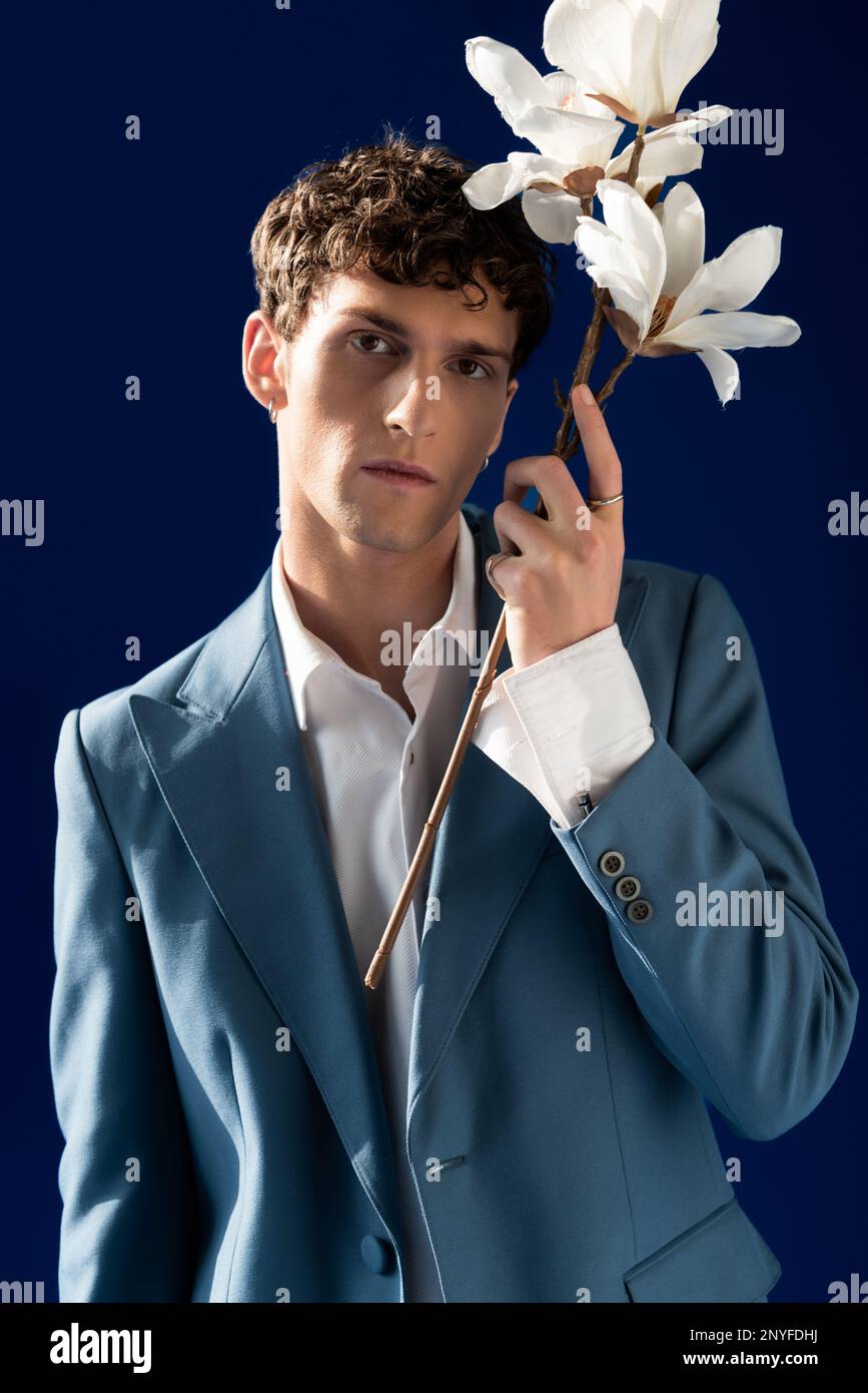 Portrait of stylish young man in jacket holding magnolia flowers ...