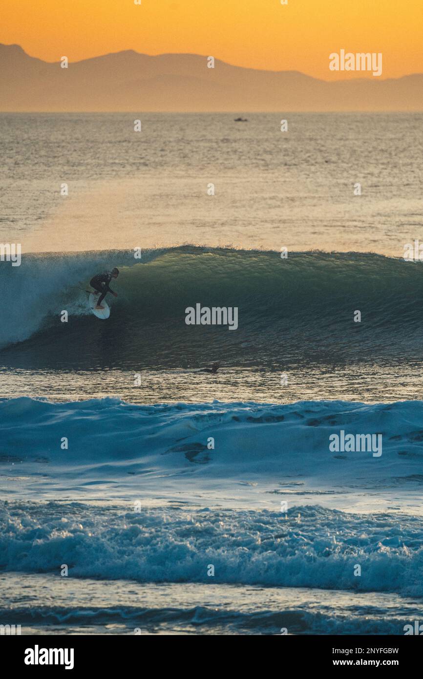 Anonymous surfer riding surfboard on foamy sea waves against mountains ...