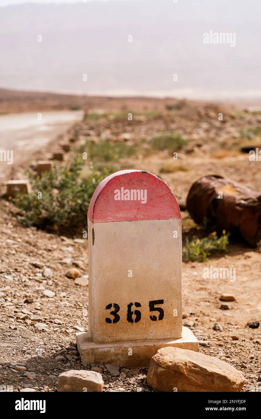 Old stone sign with numbers on rough rocky ground against road and ...
