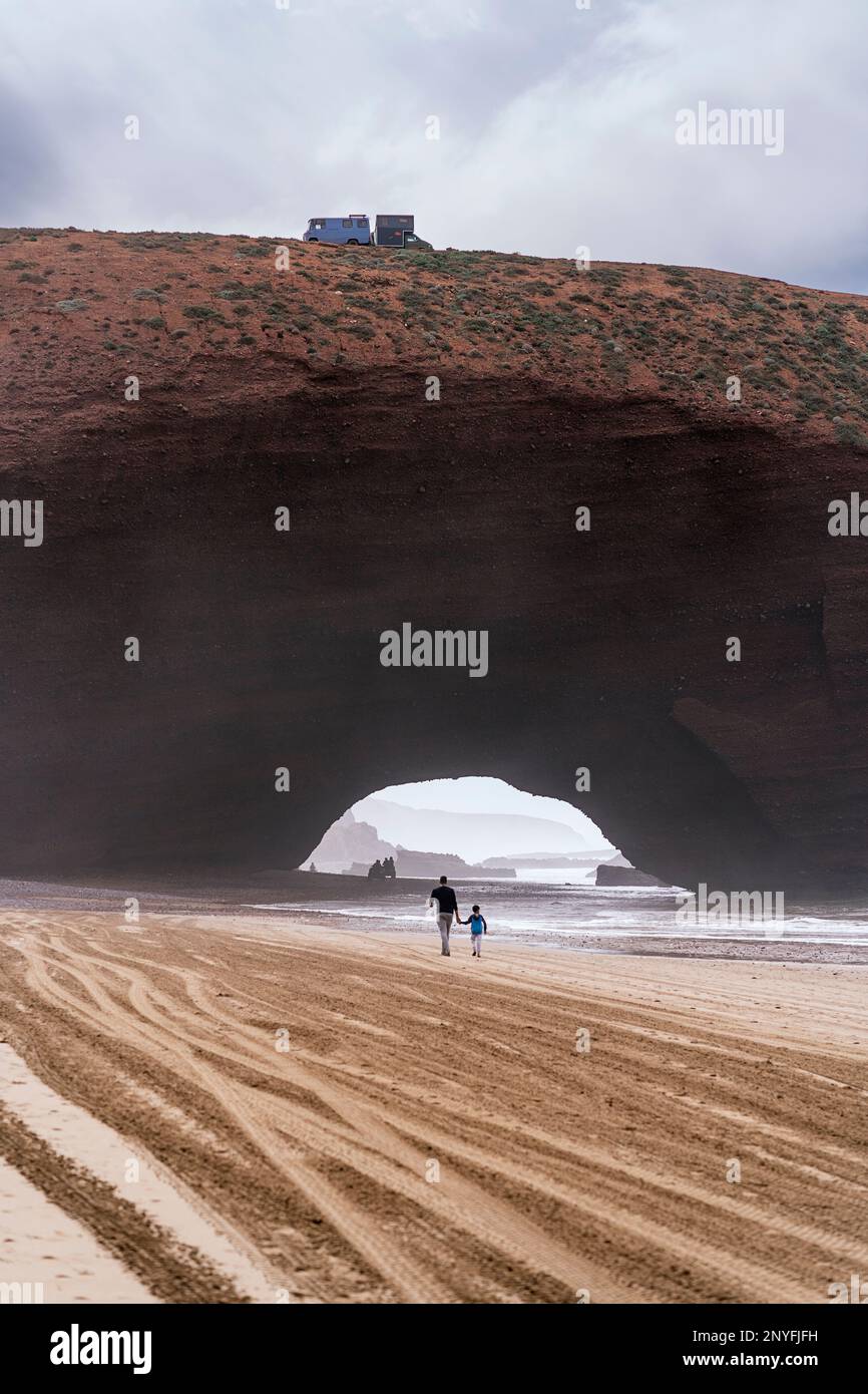 Anonymous travelers walking in sandy desert terrain under stone bridge ...