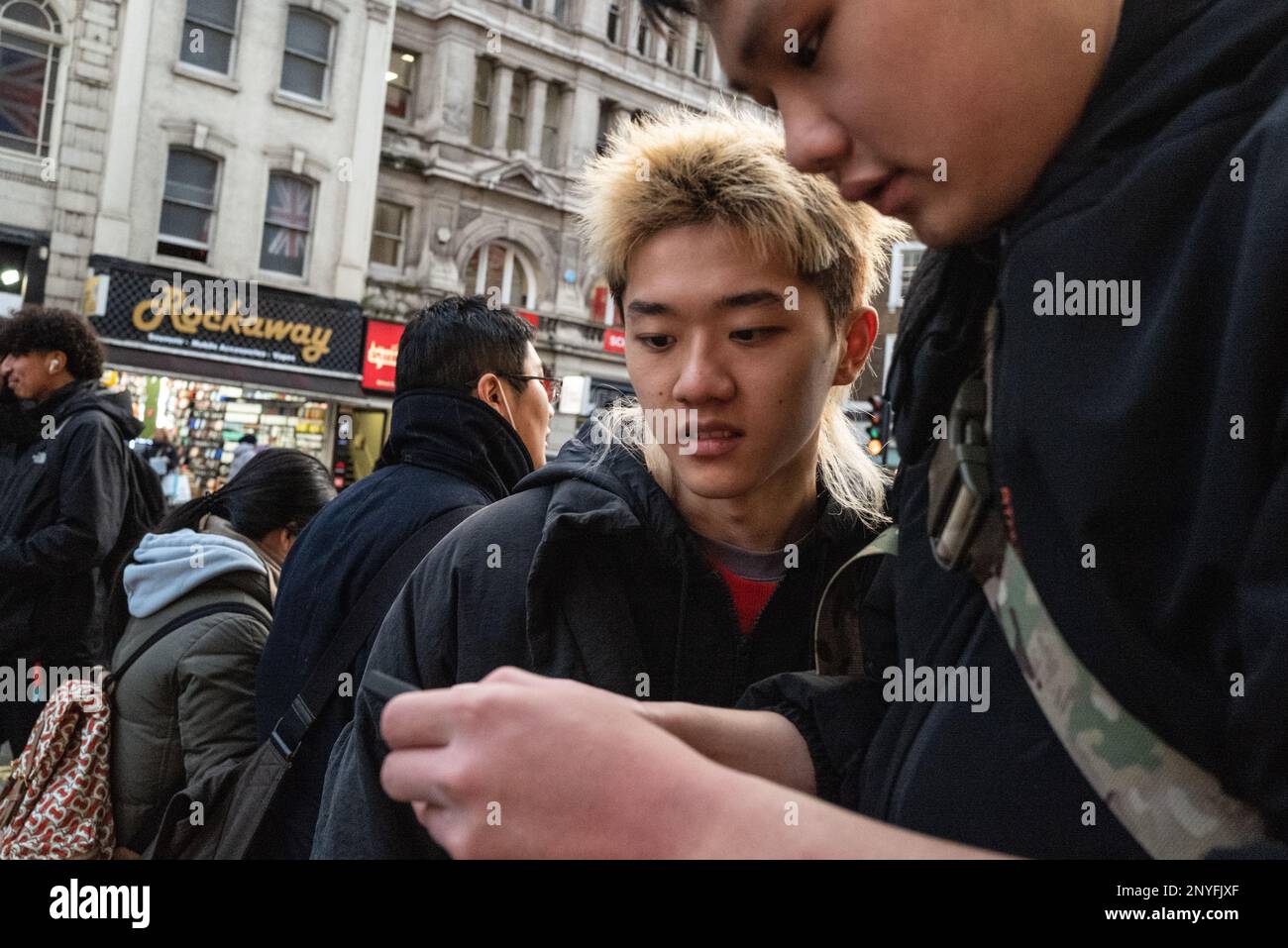 Two Asian males use a mobile/cell phone for information in city setting ...
