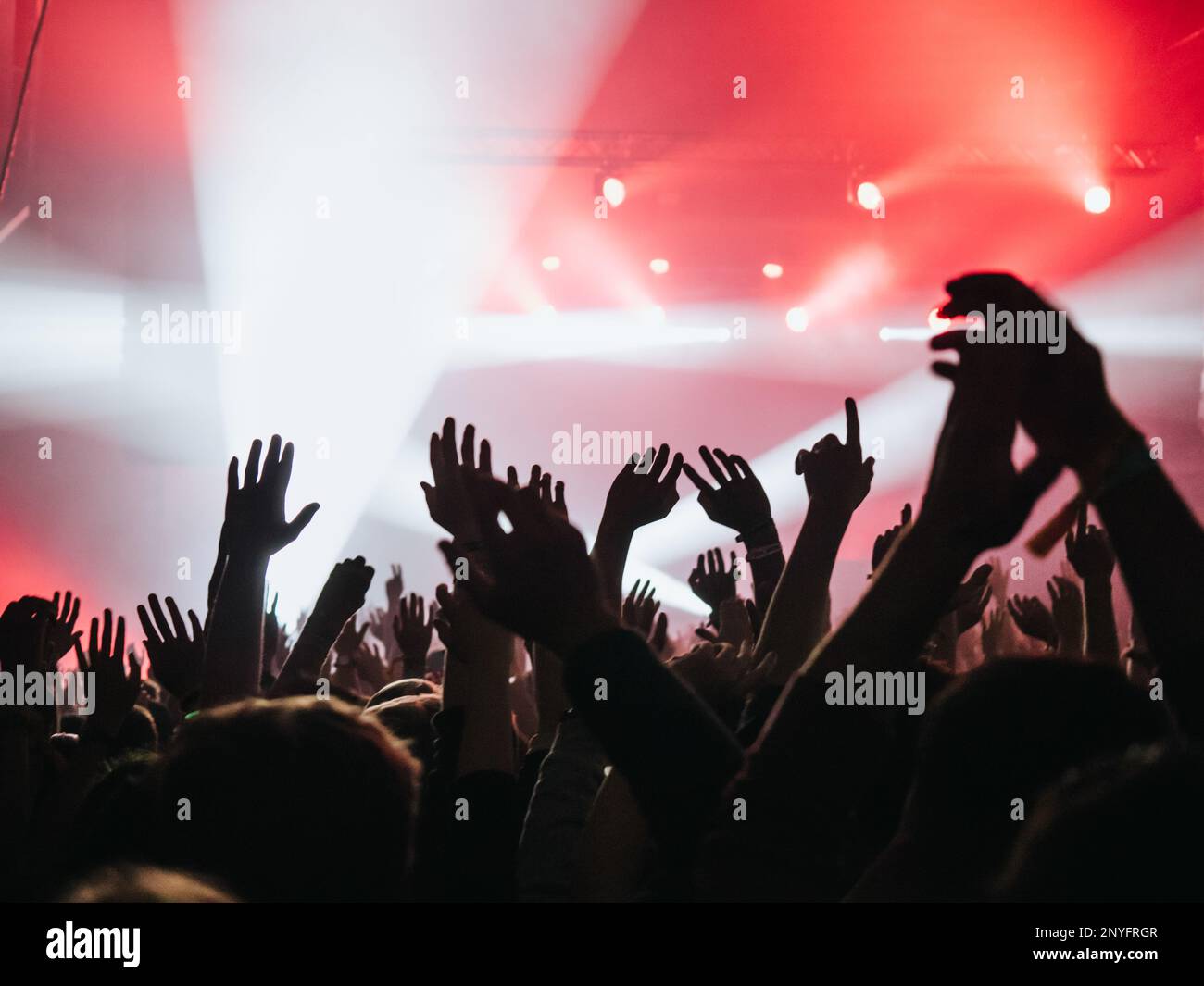 Crowd of fans raising hands under bright red light during music ...