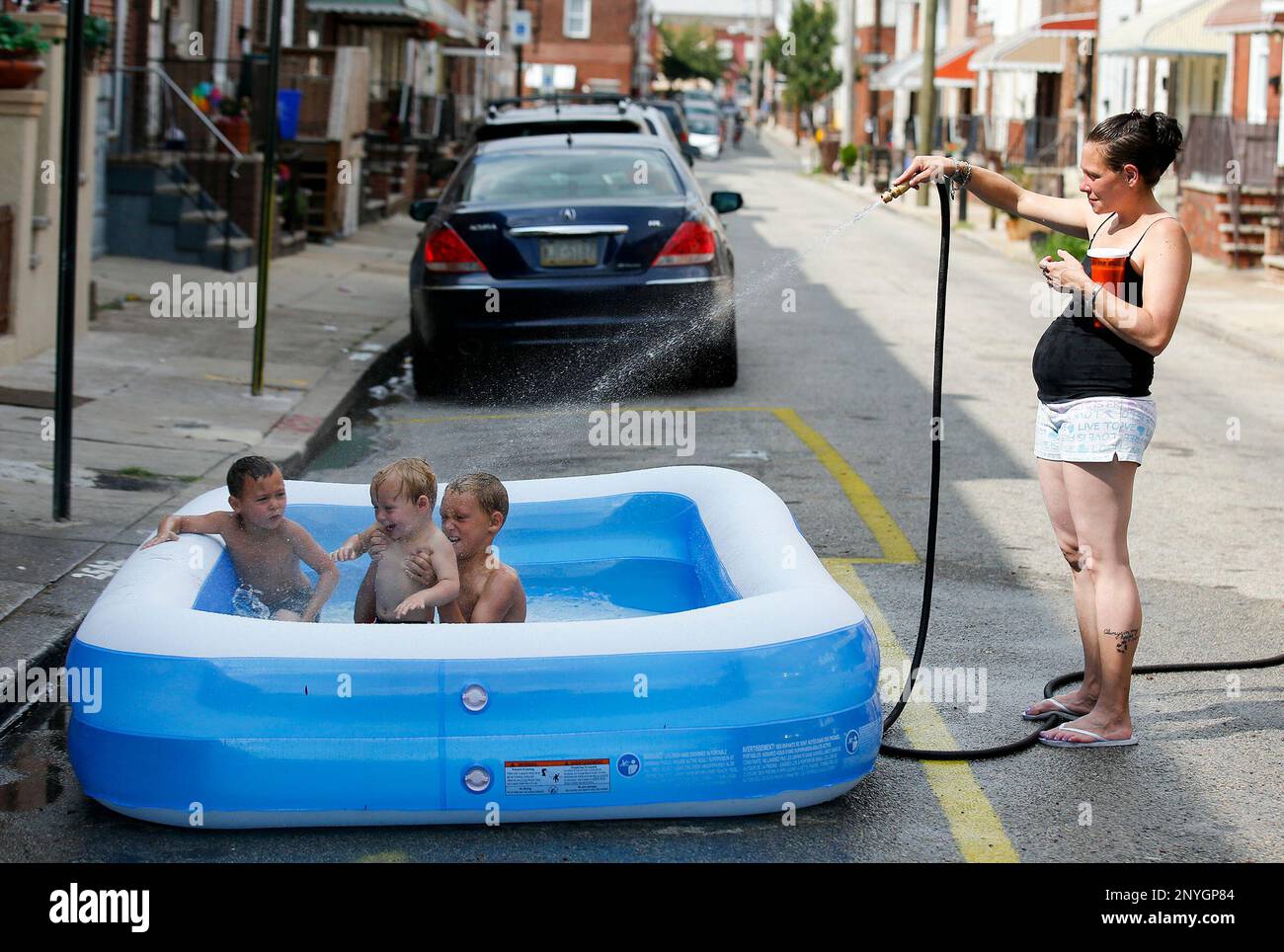 Alexis Denaro sprays water into a inflatable pool as her sons, from ...