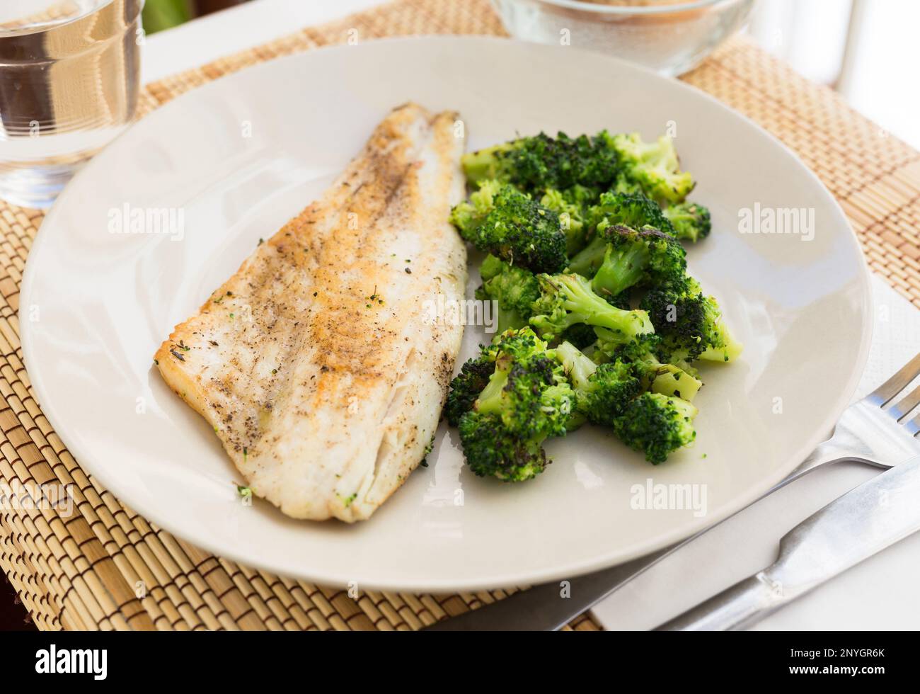 fried fillet of sea bass with garnish of broccoli on black warm stone ...