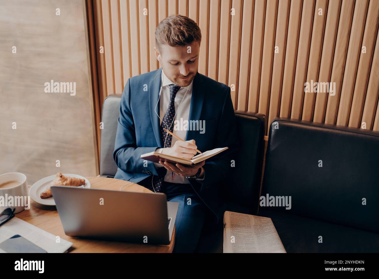 Young bearded businessman in formal wear sitting in cafe, writing down ...