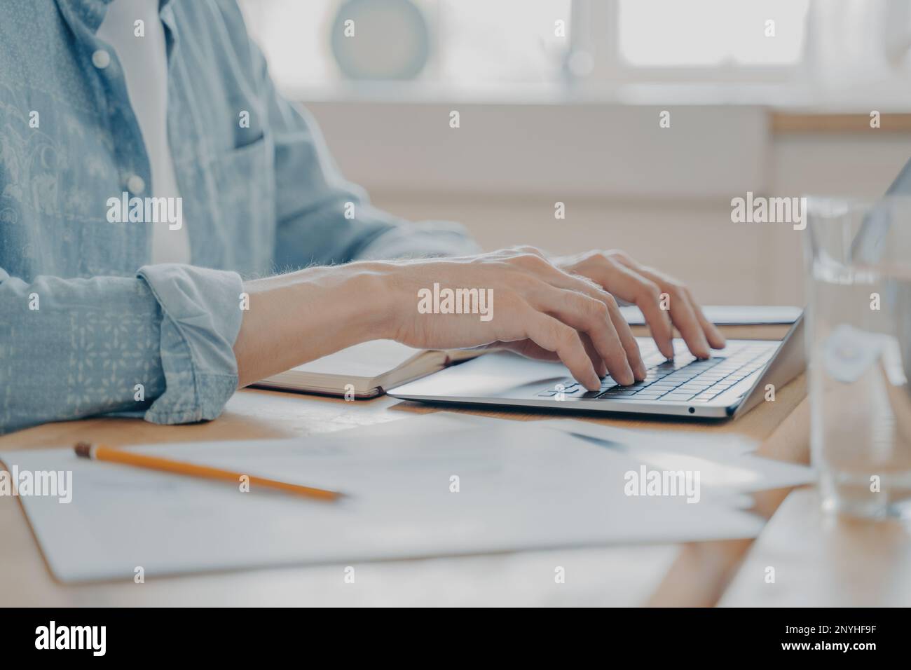 Cropped shot of man using laptop computer at home, male hands typing on keyboard on kitchen ...